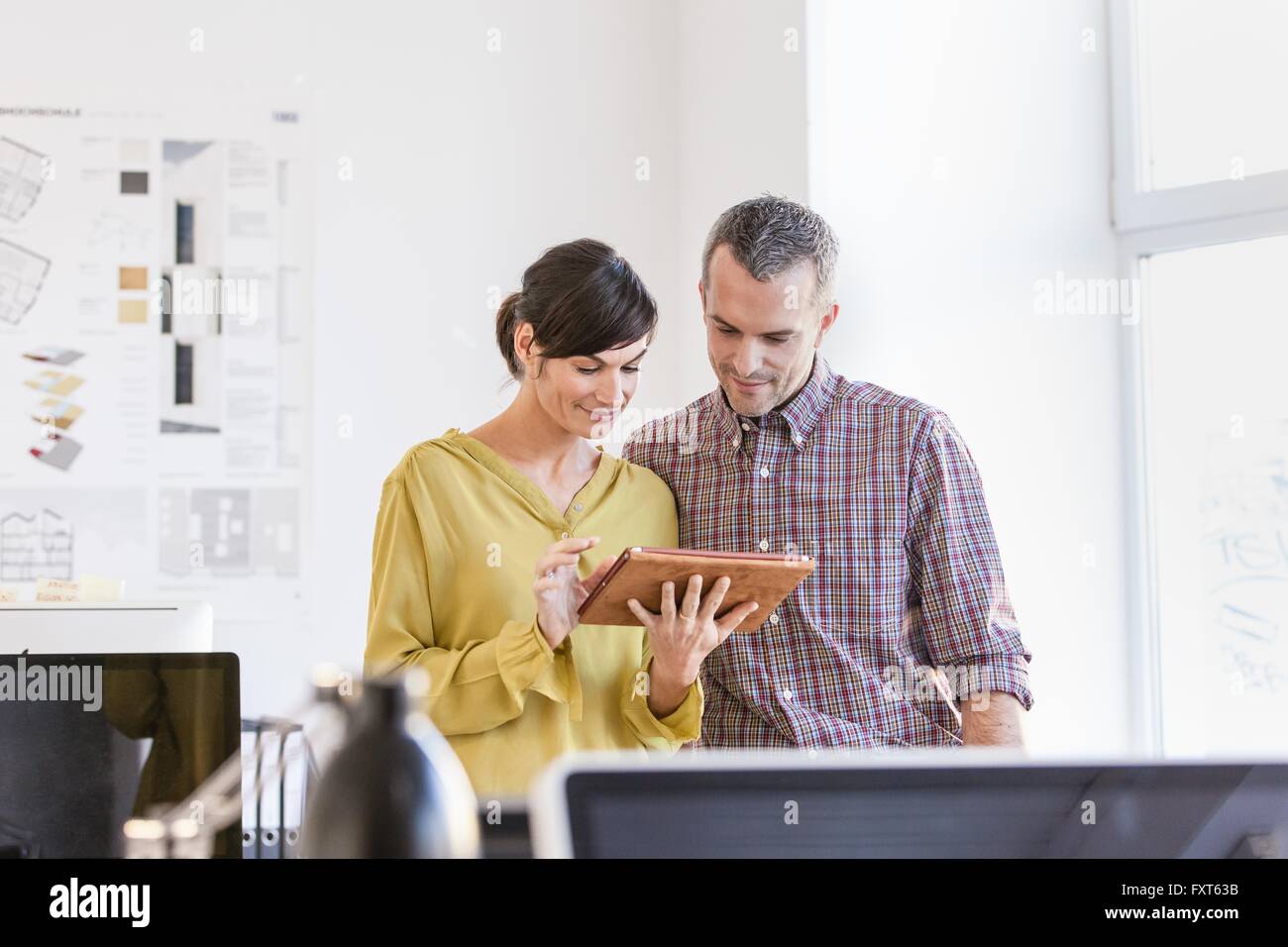Colleagues in office looking down at digital tablet smiling Stock Photo ...