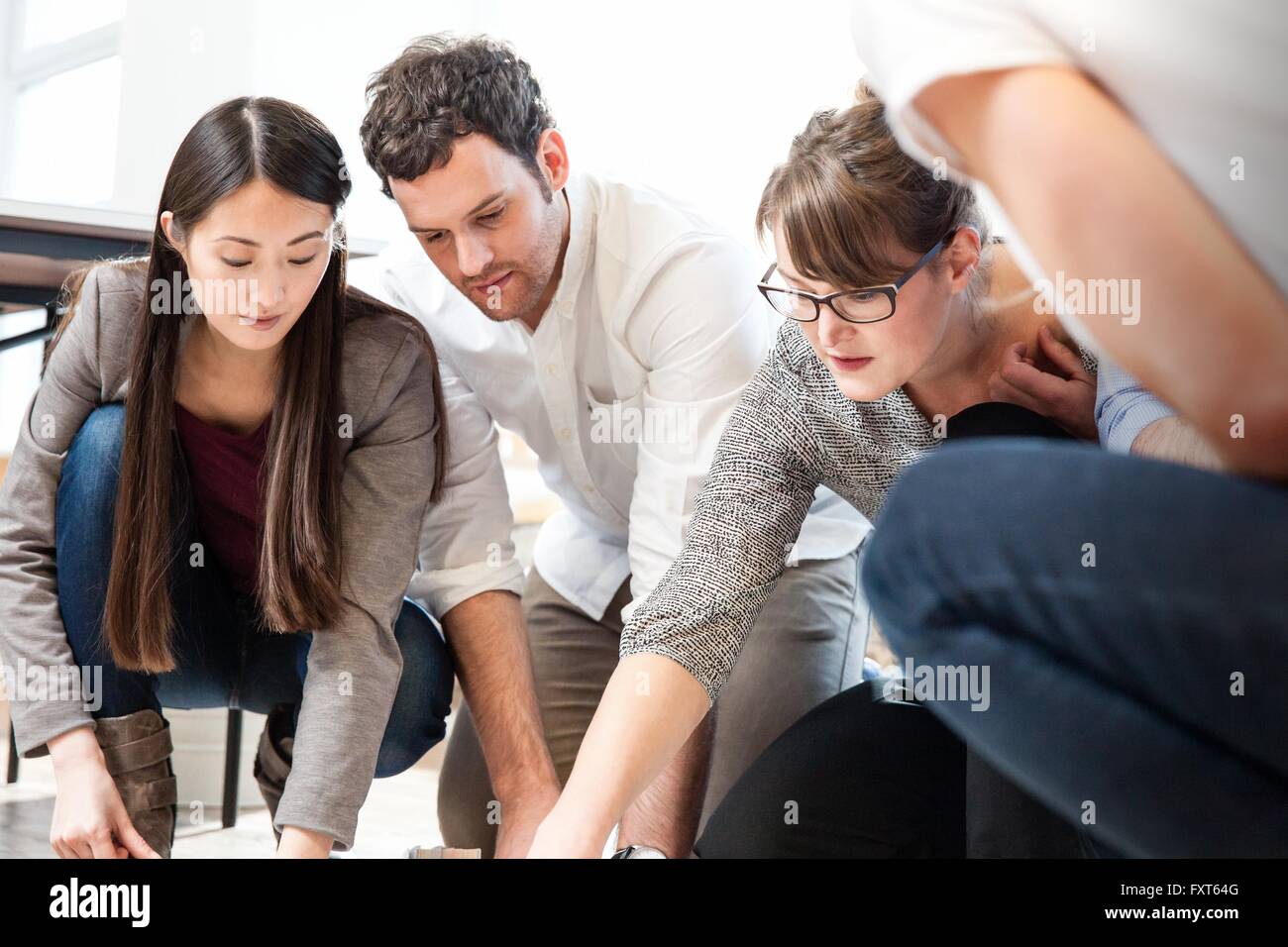 Colleagues huddled together looking down pointing at floor discussing ...