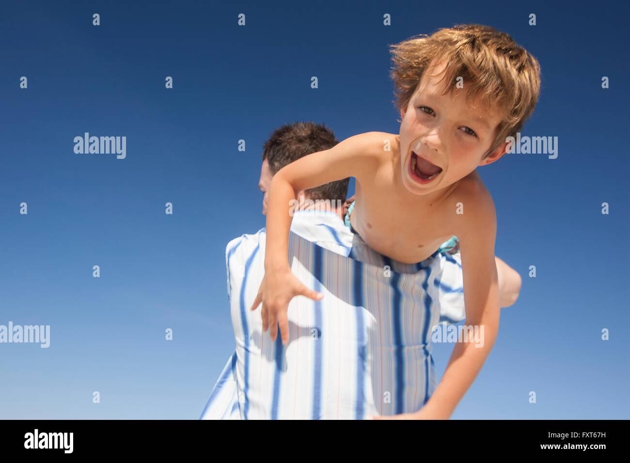 Boy being carried over fathers shoulder against blue sky Stock Photo ...