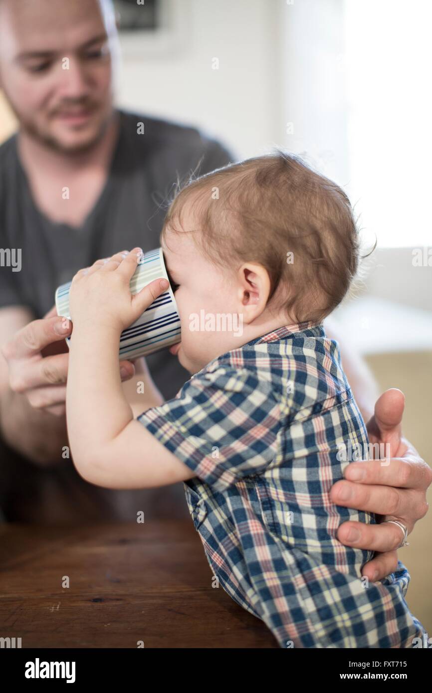 Father helping baby boy to drink from mug Stock Photo - Alamy