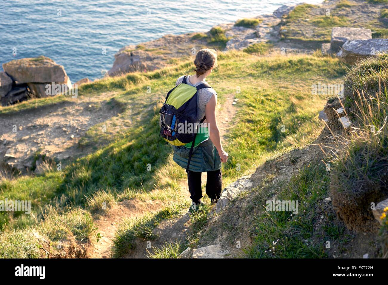 High angle rear view of hiker with backpack hiking down cliff side ...