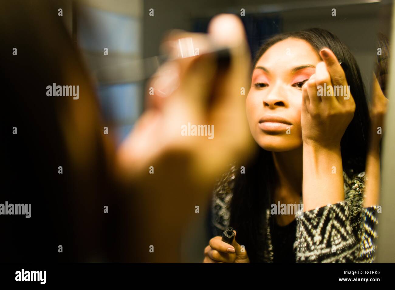 Over shoulder mirror image of young woman putting on eye shadow in ...