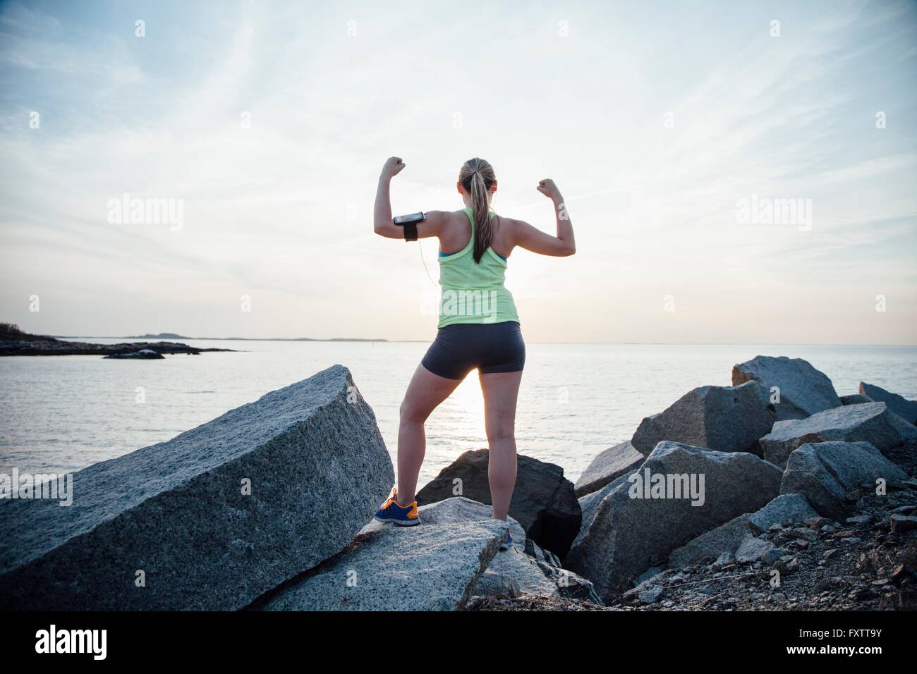 Rear view of woman standing on rocks arms raised flexing muscles Stock ...