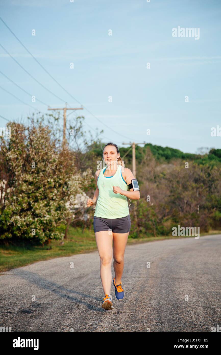 Full length front of woman wearing activity tracker jogging on road ...
