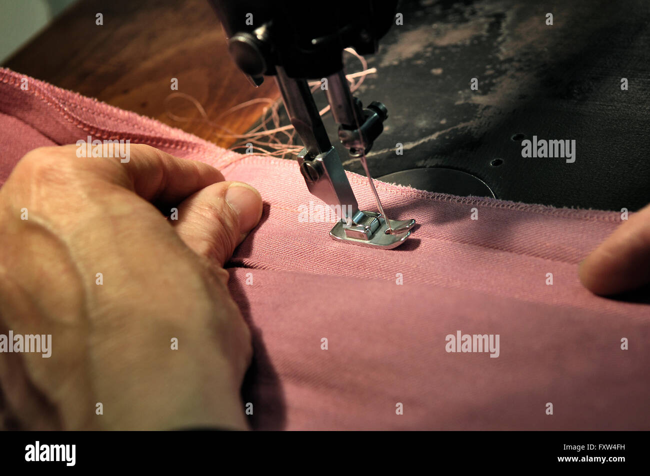 A hand of a dressmaker supporting a cloth while sewing on a sewing ...