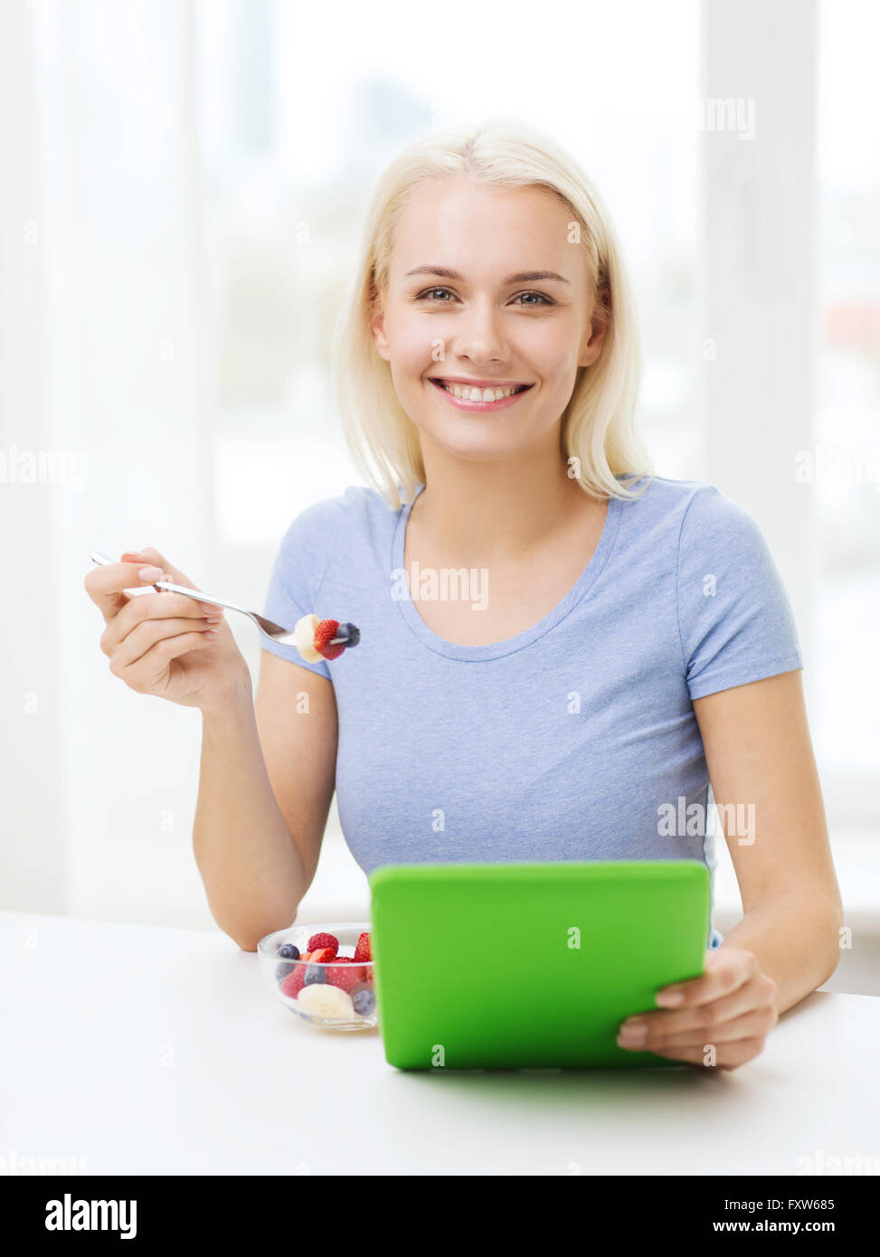 smiling woman eating fruits with tablet pc at home Stock Photo - Alamy