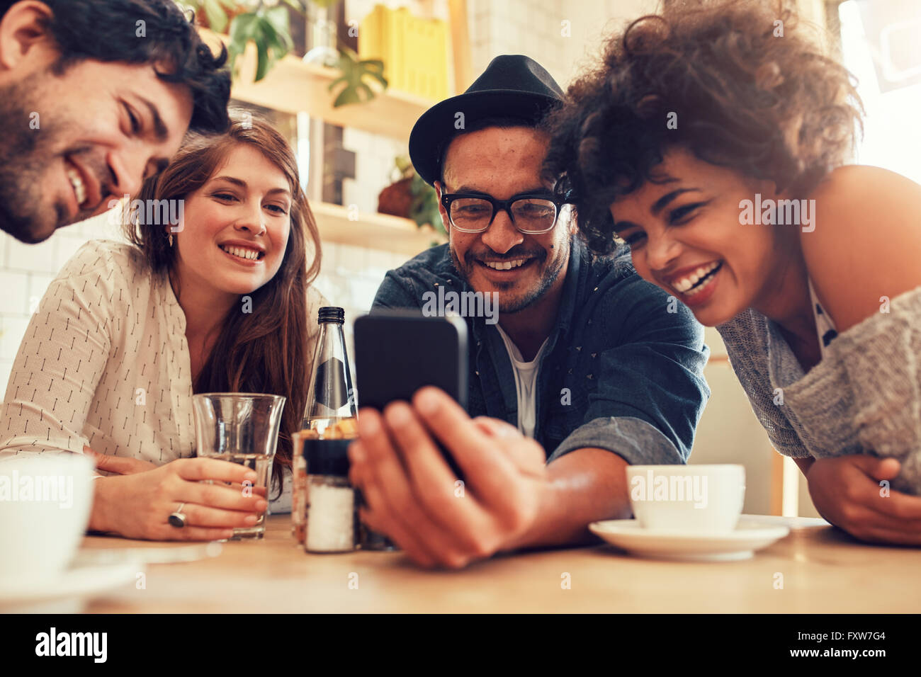 Group of friends sitting together in a cafe looking at mobile phone and ...