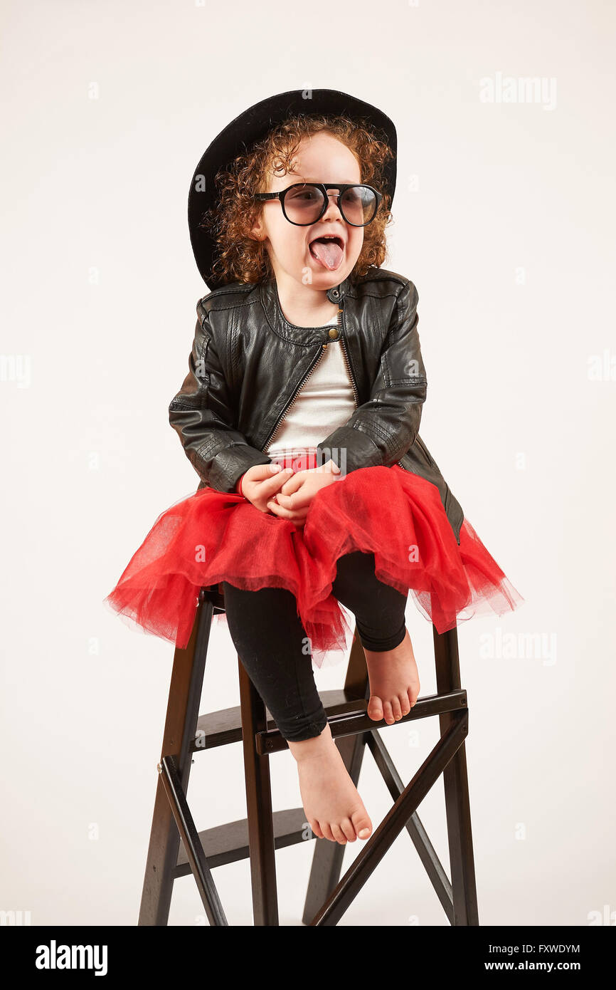 Little girl with black hat and sunglasses sitting on a high stool and ...