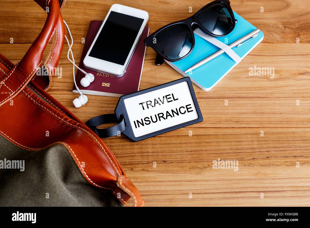 Travel bag with insurance tag and tourist accessories on wood table ...