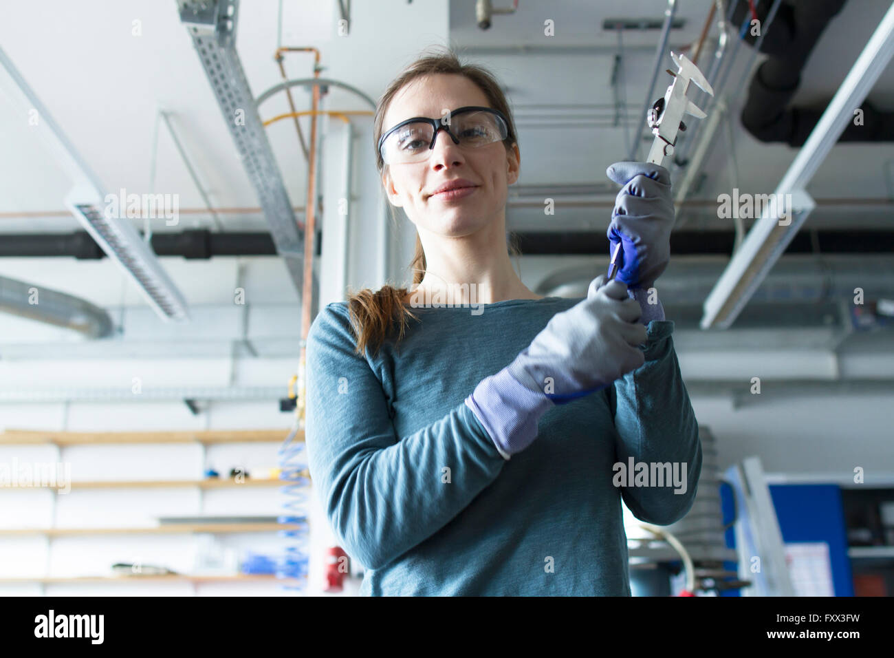Low angle view of woman in workshop wearing safety goggles holding tool ...