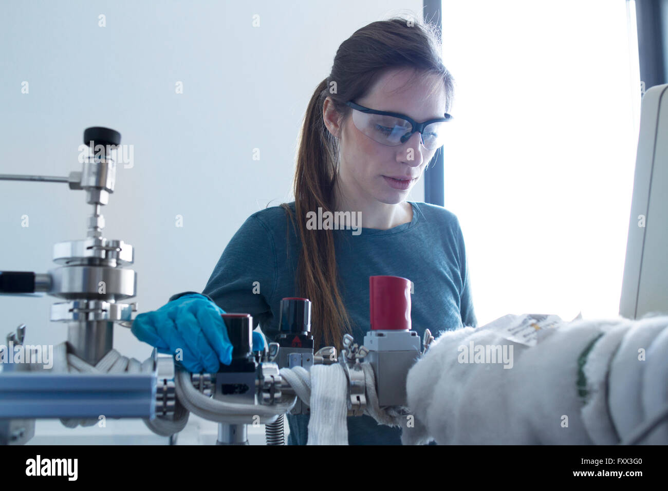 Woman in workshop wearing safety goggles adjusting machine Stock Photo ...