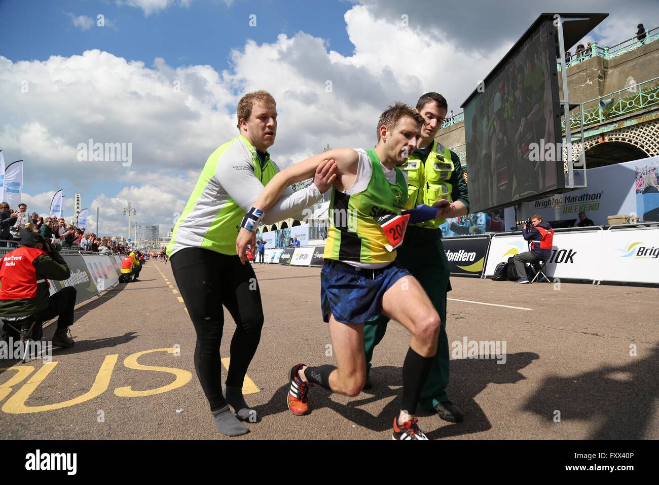 A paramedic and official helps a exhausted runner reach the finish line ...
