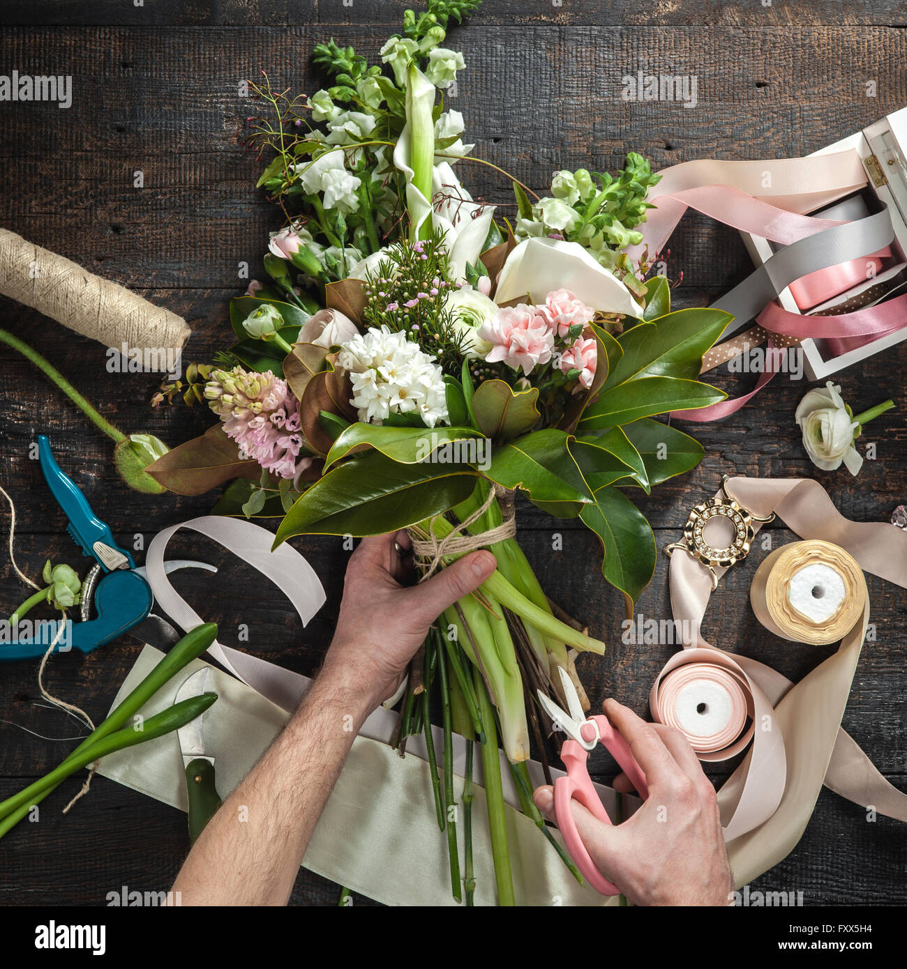 The hands of florist against desktop with working tools and ribbons on ...
