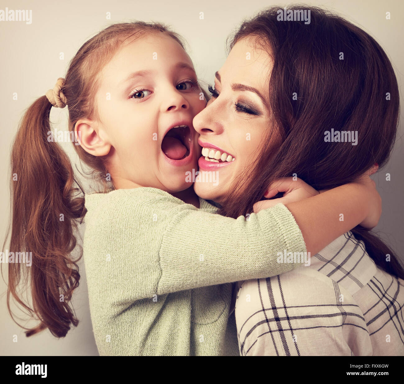 Happy grimacing kid wanting to biting her laughing mother in nose with ...