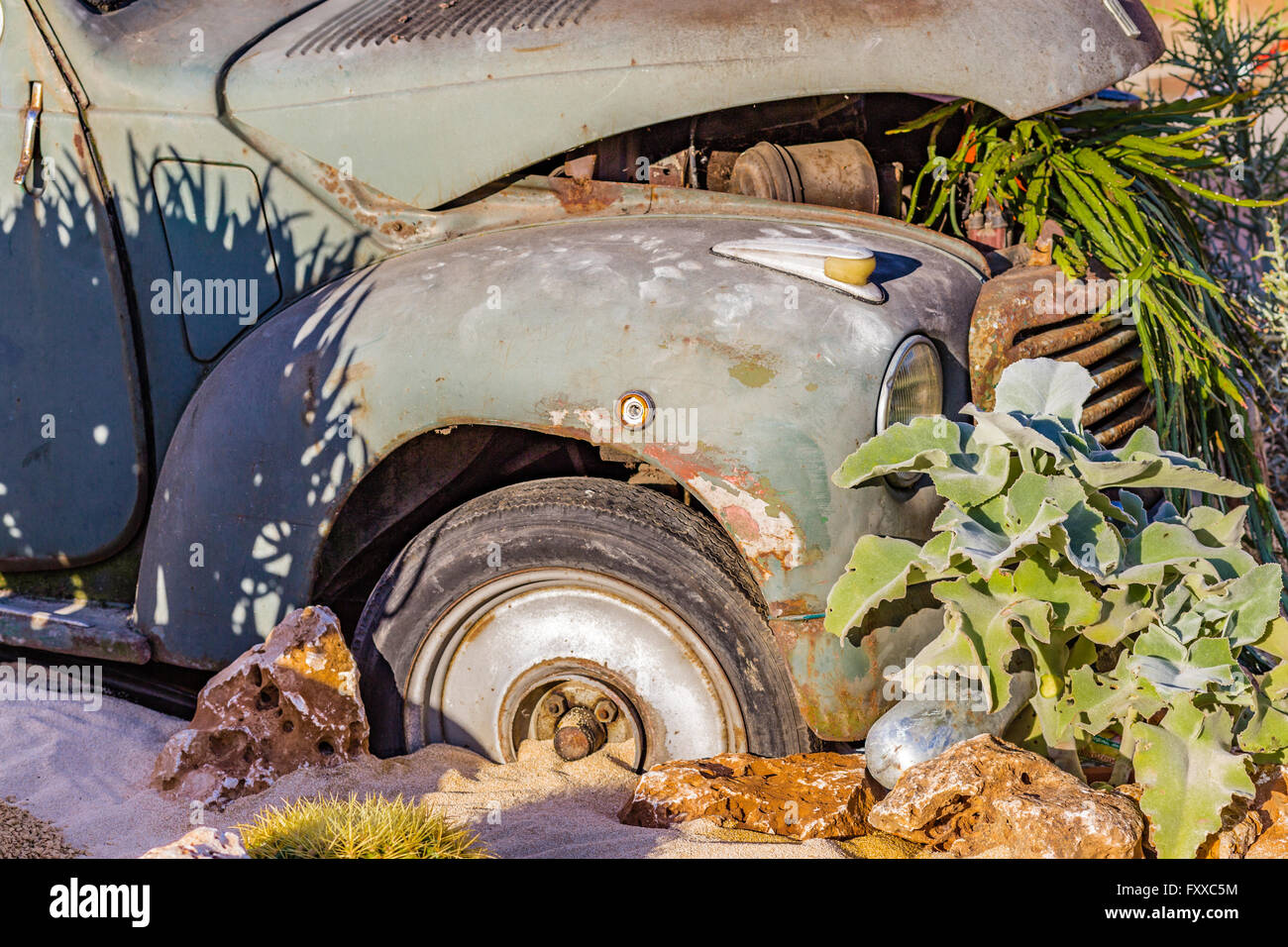carcass of an old rusty car in the desert sand surrounded by rocks and ...