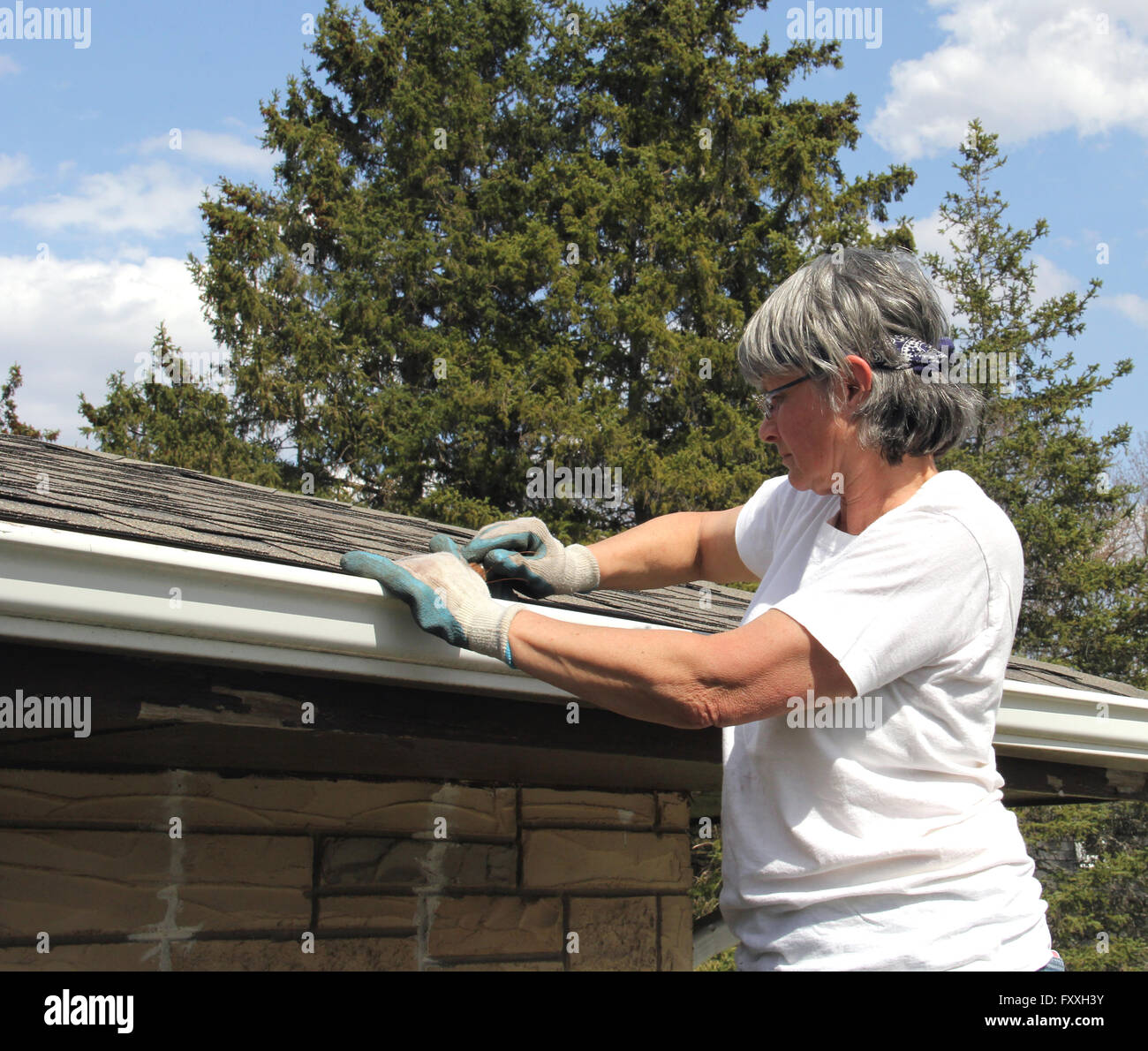 Woman on a ladder cleaning rain gutters with a blue sky in the ...