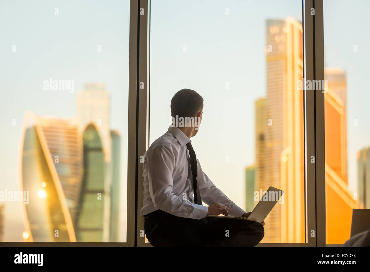 Morning in business office. Back view of young man sitting on window ...