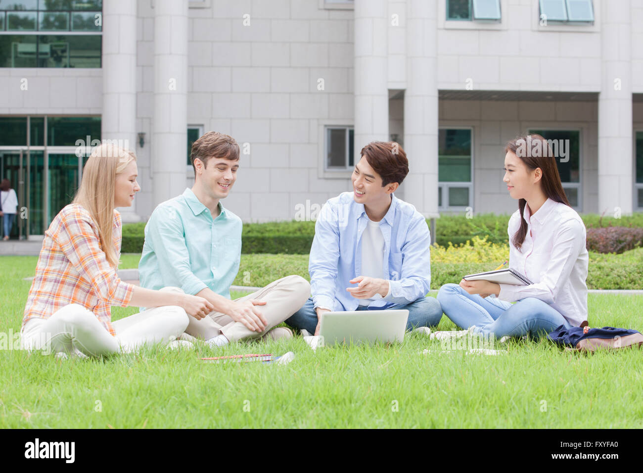 Domestic and international college students seated on a grass on campus ...