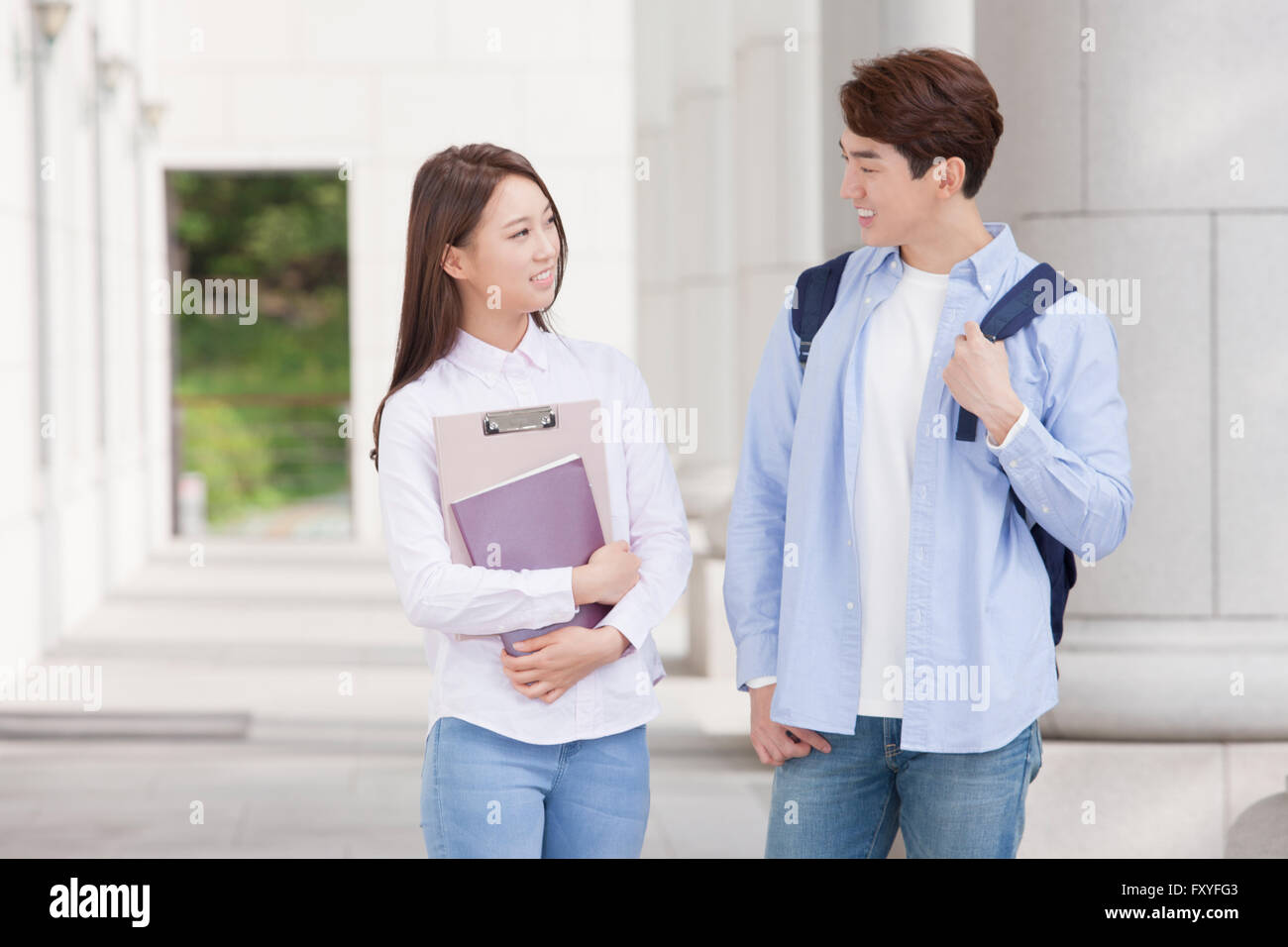 Campus couple with backpack and books looking at each other and having a conversation on campus ...