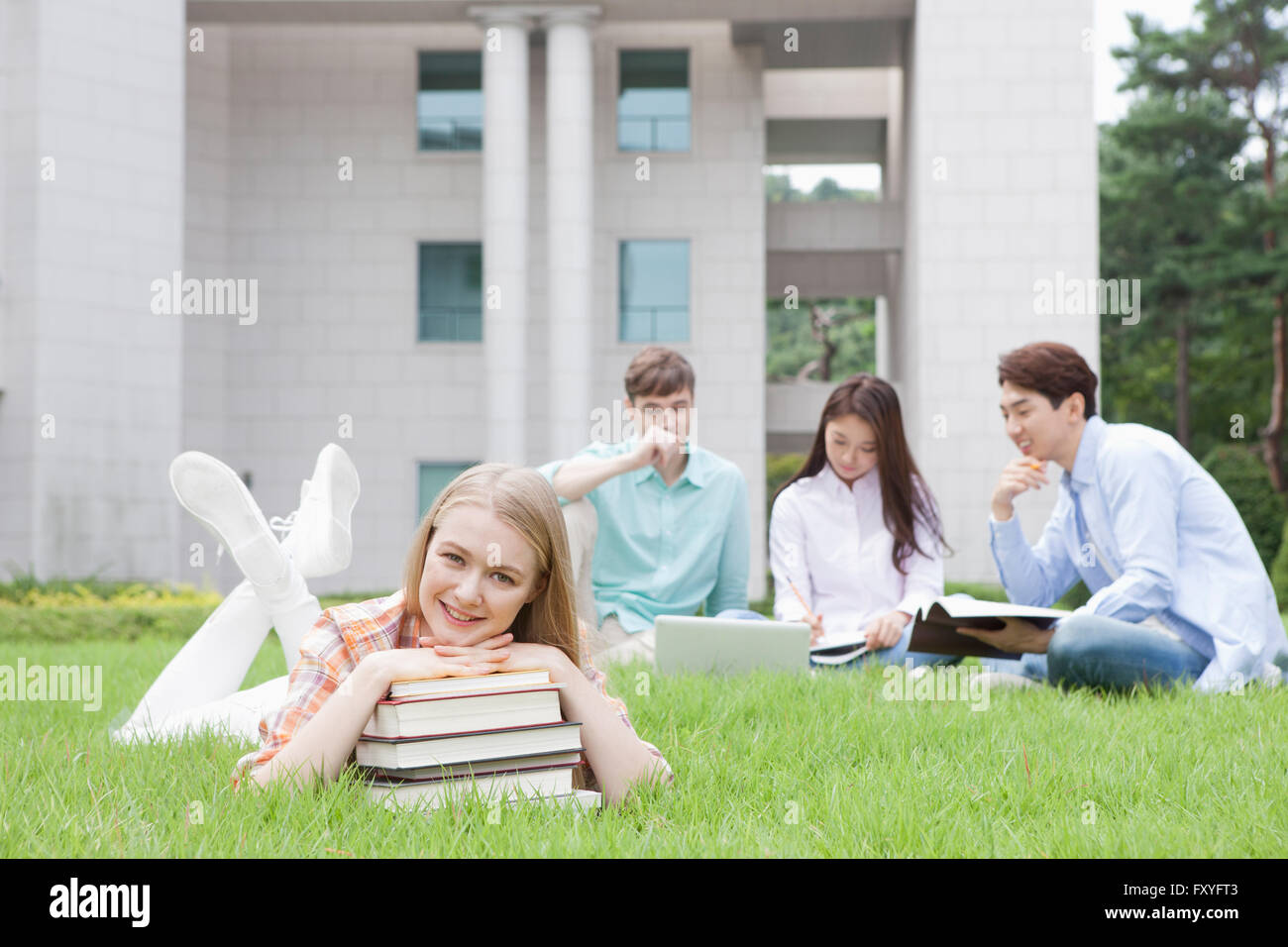 International student in college lying on her front on a grass with her ...