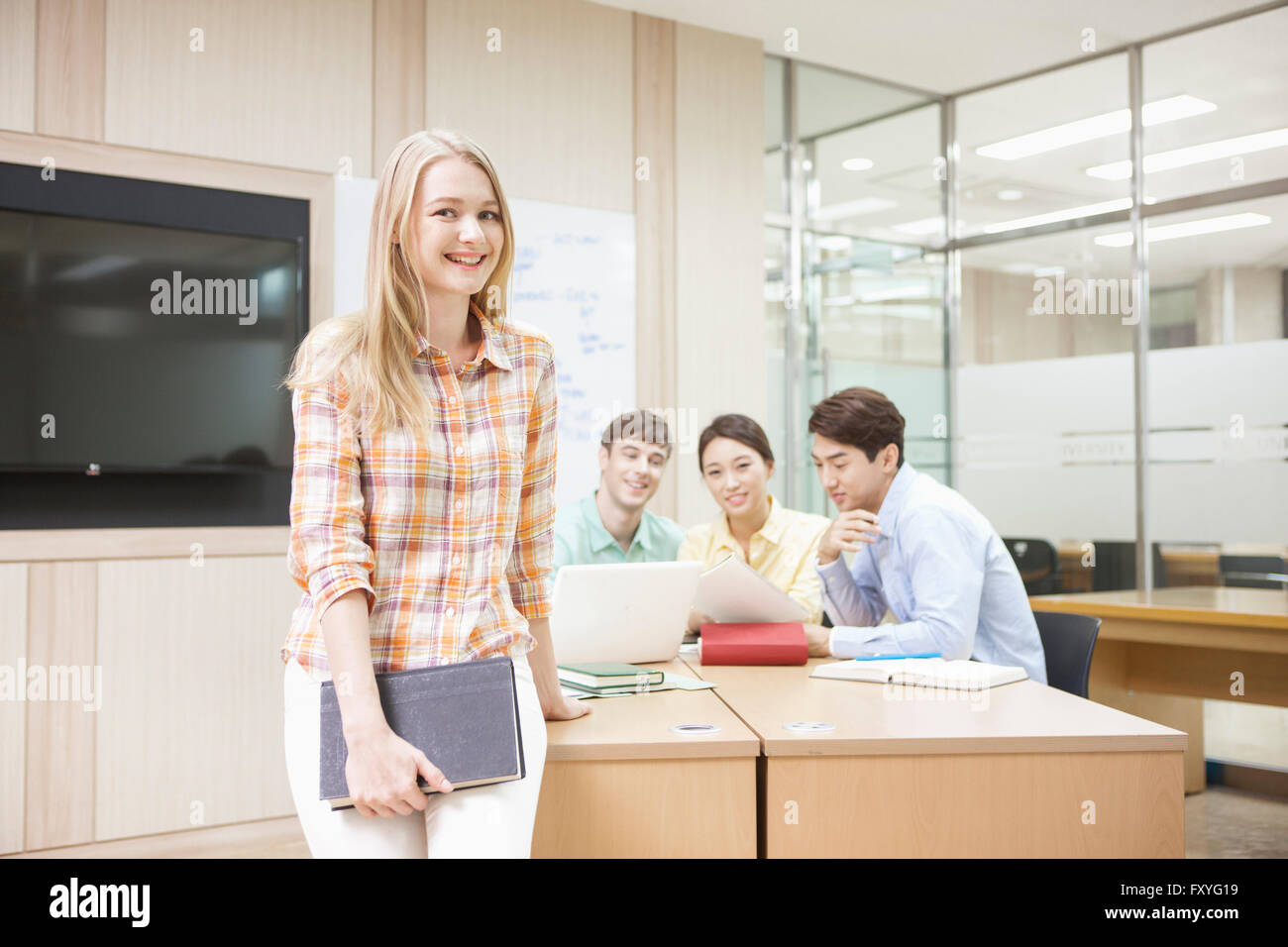 International student leaning on a desk with a book in her arms and ...