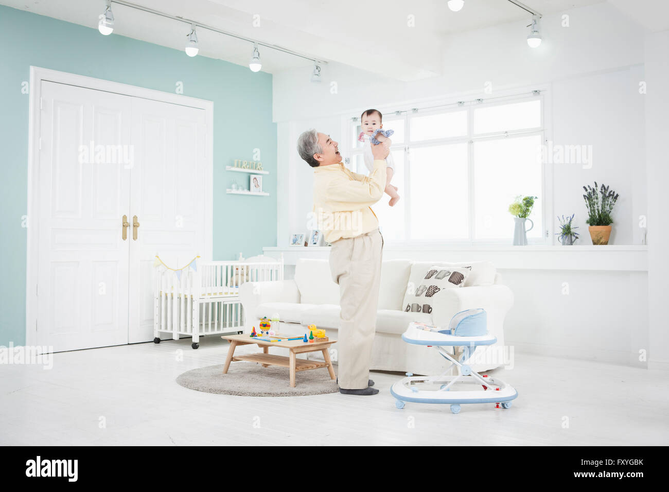Senior man standing and holding a baby high in a room and taking care ...