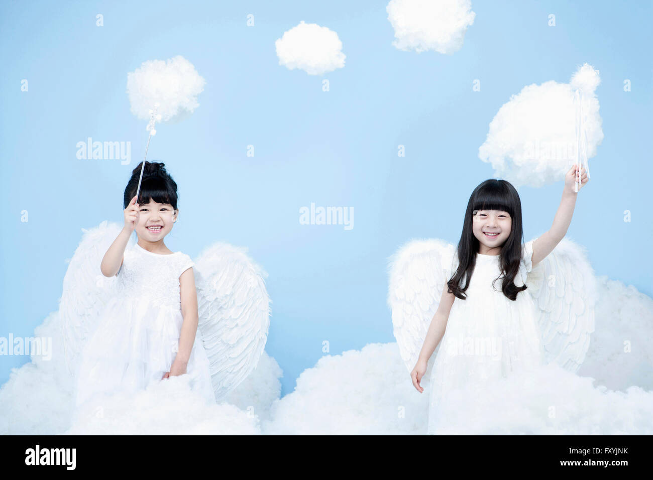 Two girls in angel costume holding magic stick each and smiling in the ...