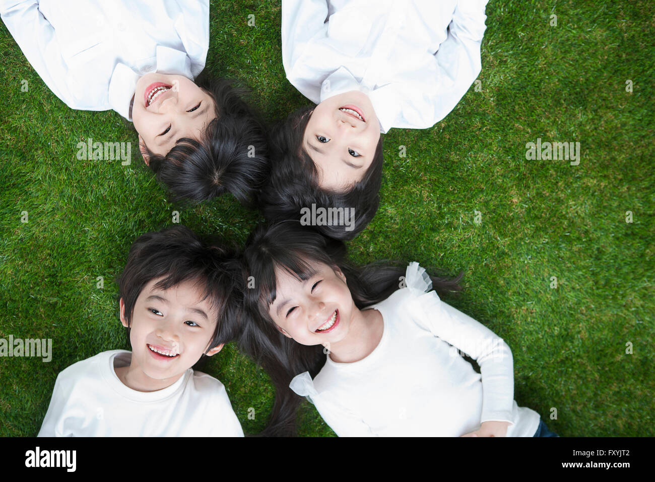 Four children lying on grass and smiling Stock Photo - Alamy