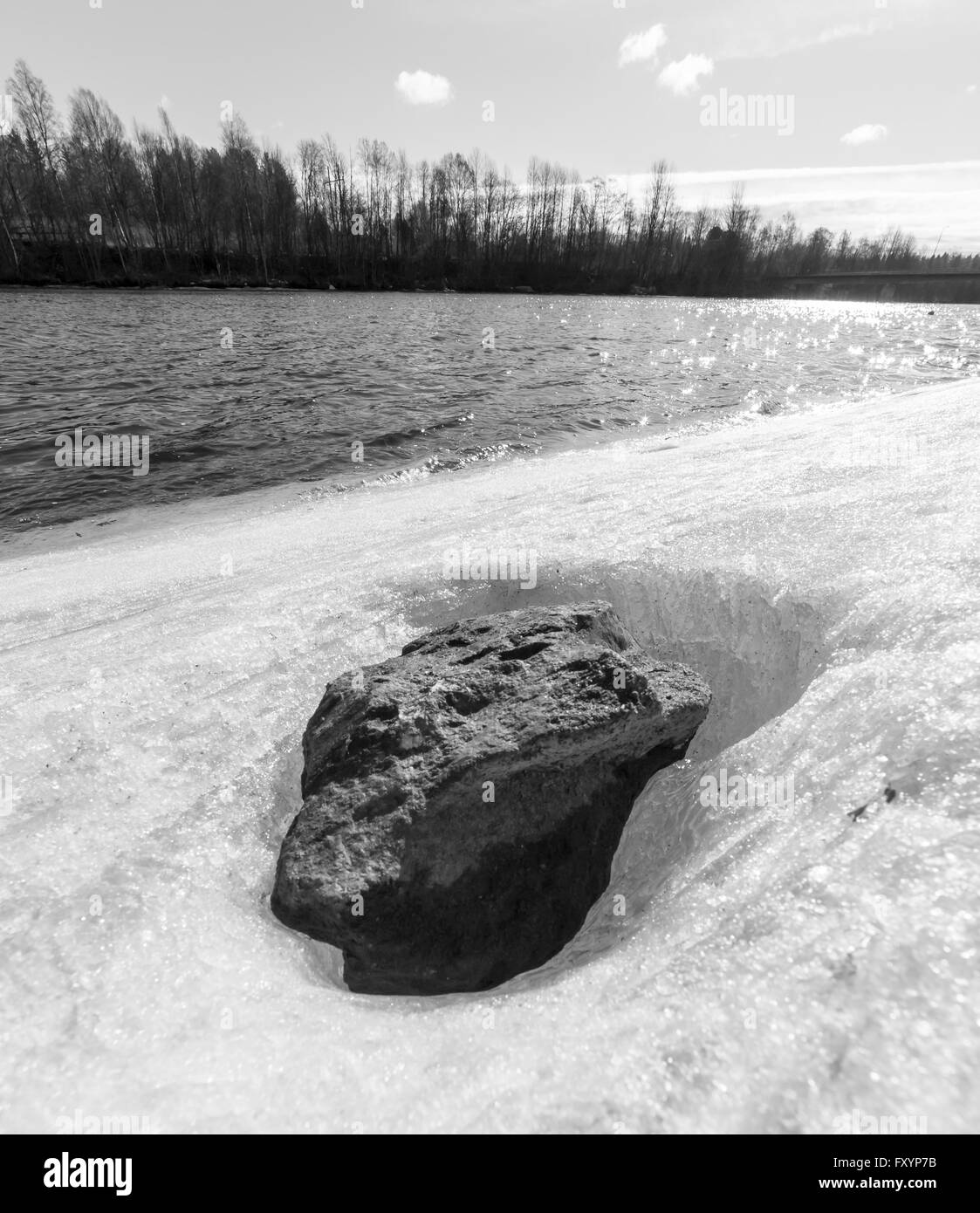 Stone in Ice by River with trees and a partly cloudy sky Stock Photo ...