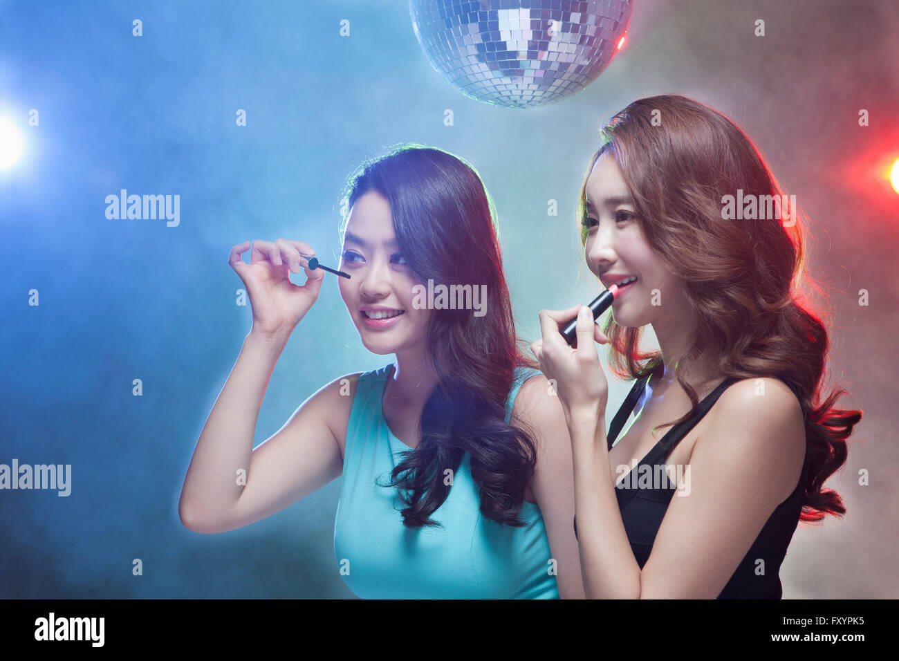 Side view of two young smiling women putting on make up at nightclub ...