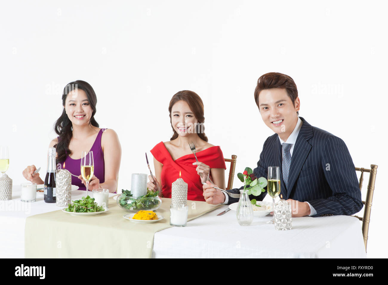 Portrait of three young smiling people sitting at party table starting ...