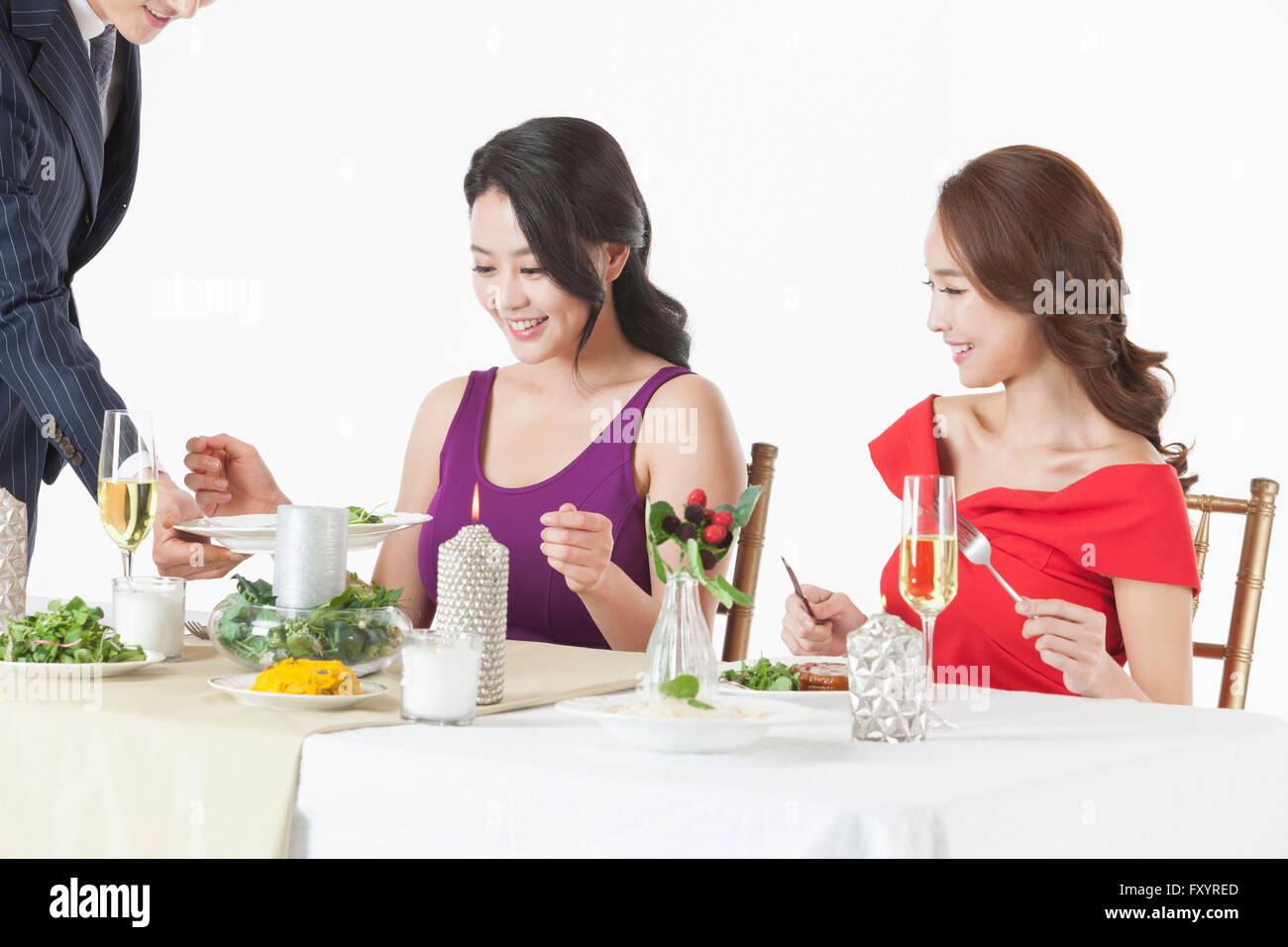 Portrait of two young women sitting at table served by young man Stock ...