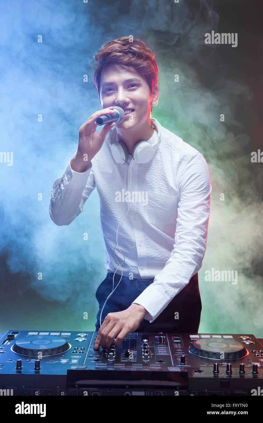 Young smiling male DJ holding a microphone playing music at nightclub ...