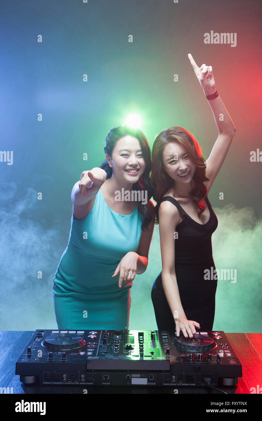 Two young smiling women dancing playing music at nightclub staring at ...
