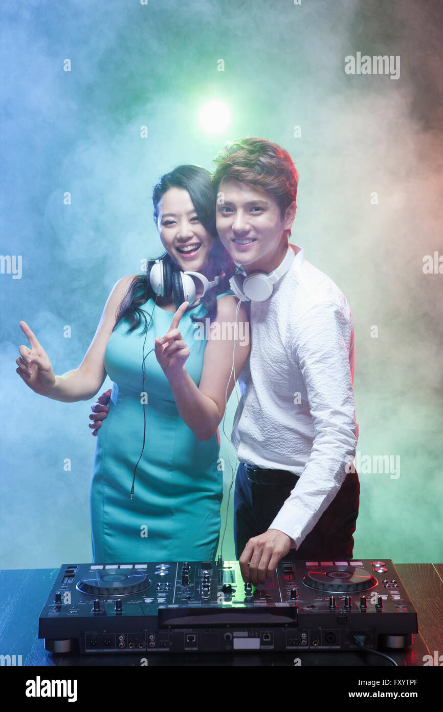 Two young smiling DJ couple hugging playing music staring at front at ...
