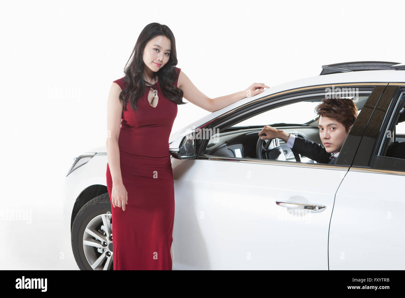 Young woman in red dress posing in front of car and young man in suit ...