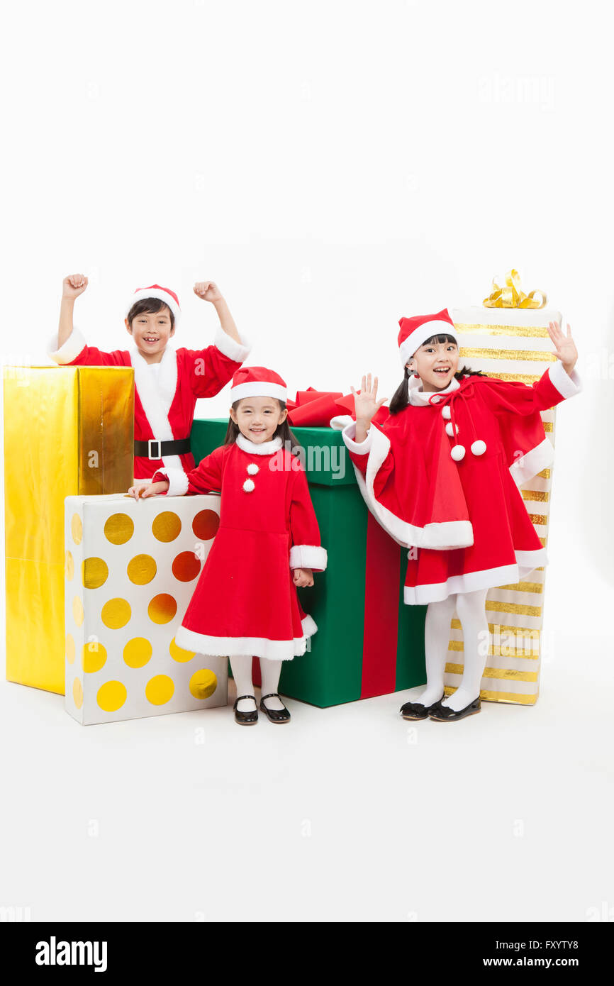 Three smiling children in santa's clothes with present boxes staring at ...