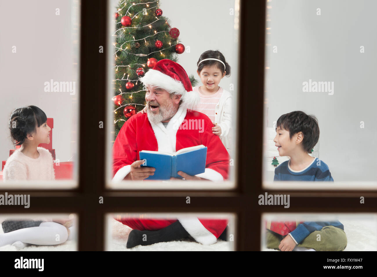 Smiling Santa Claus reading a book to smiling children at Christmas ...