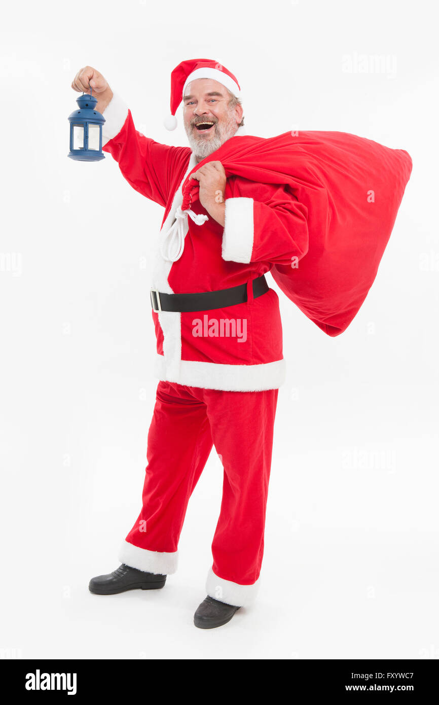 Side view of smiling Santa standing with a lantern and present bag ...