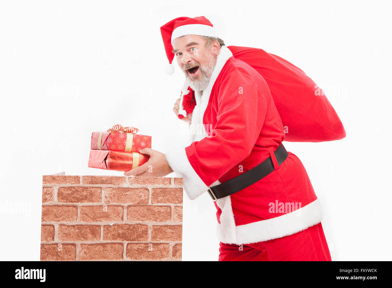 Side view of smiling Santa holding present boxes at chimney staring at ...