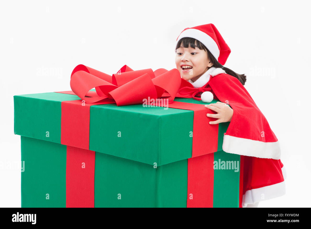 Side view of smiling girl in santa's clothes hugging a big present box ...