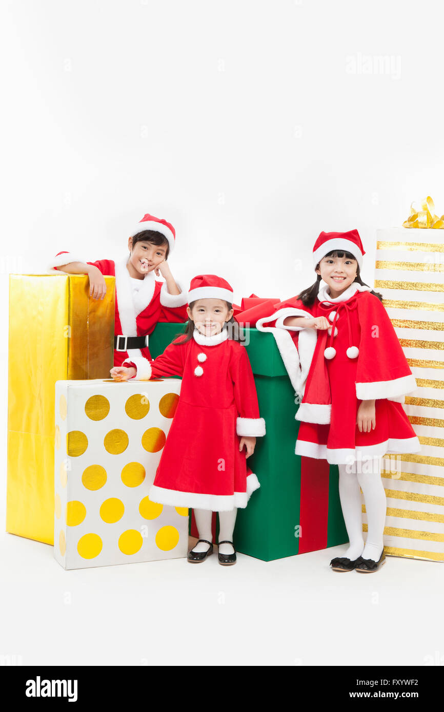Three smiling children in santa's clothes posing with stacked present ...