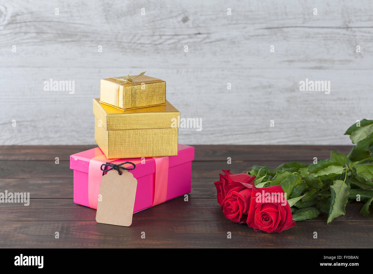 Three red roses and three gift boxes with empty tag on wooden table ...