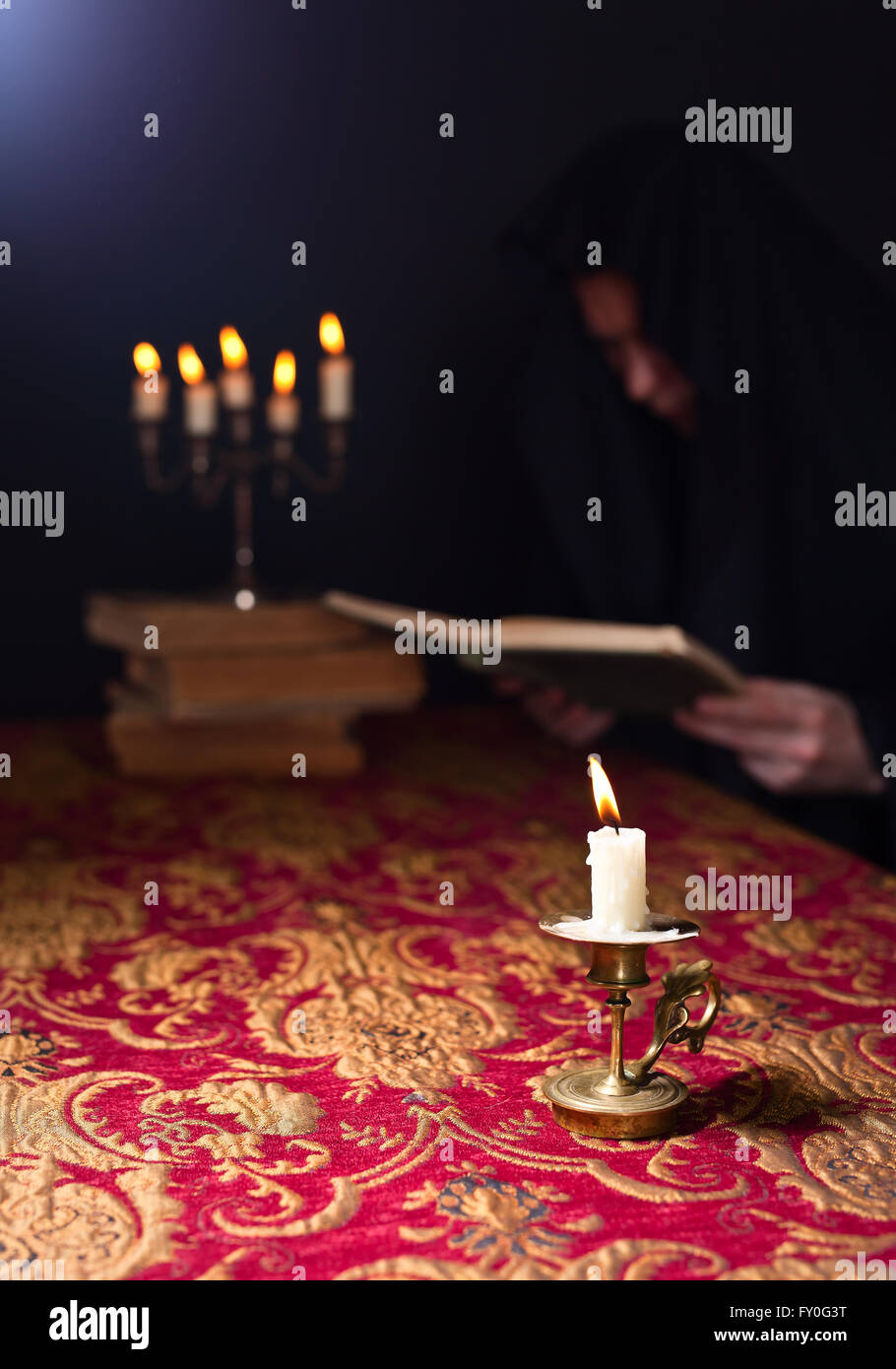 Candle in a small candlestick and reading monk Stock Photo - Alamy