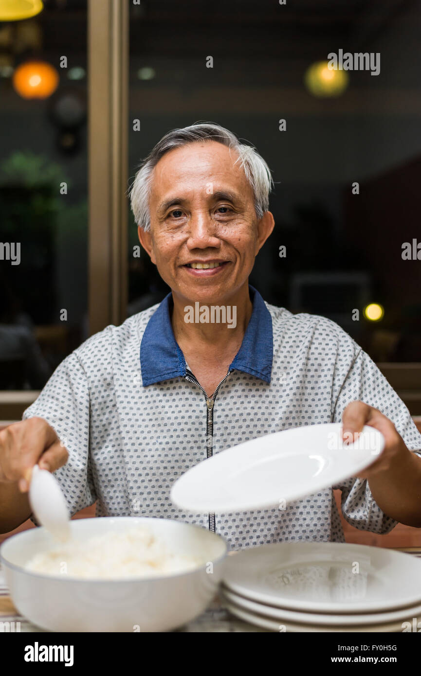 Happy smiling Asian male senior serving rice onto plate Stock Photo - Alamy