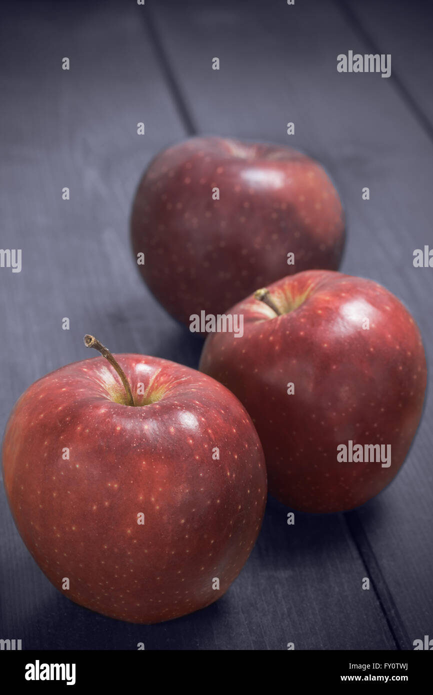 Three red apples are standing on a wooden table. Edited as a rustic ...
