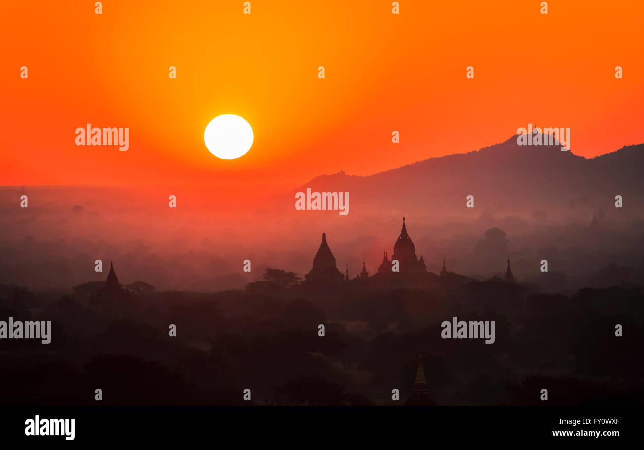 Sun rising over the horizon and temples in morning mist, at Old Bagan ...