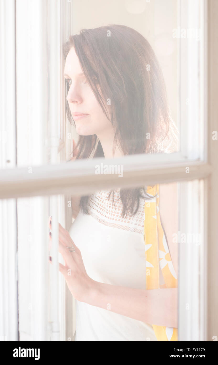 Woman standing by a window, looking away. Concept of sadness, waiting ...