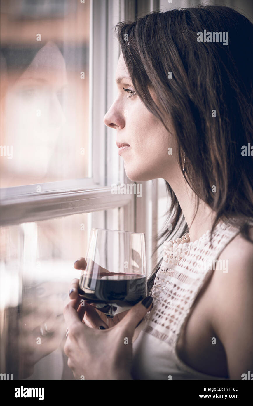 Woman standing by a window, looking away. Concept of sadness, waiting ...