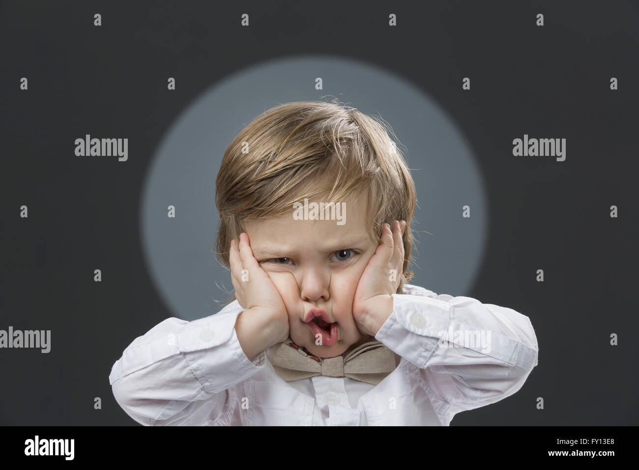 Portrait of cute boy pressing cheeks against gray background Stock ...